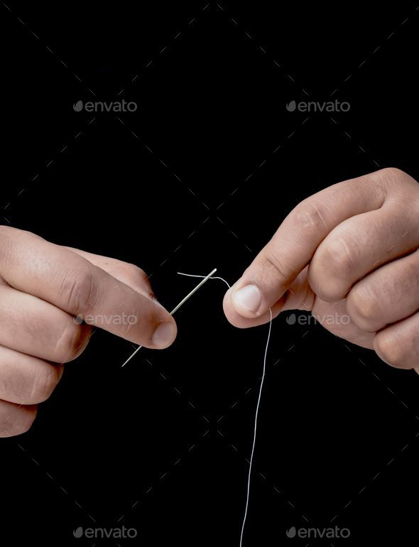 Male hands skillfully threading a needle on a solid black background ...