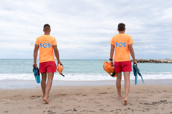 Lifeguards walking with a float on a beach watch Stock Photo by riderfoot