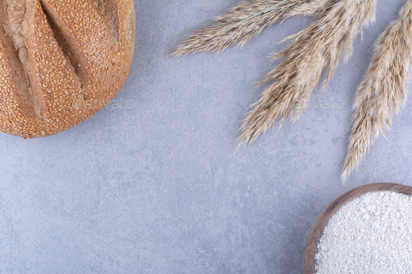 Stalks of dried feather grass, bread loaf and a flour bowl on marble ...