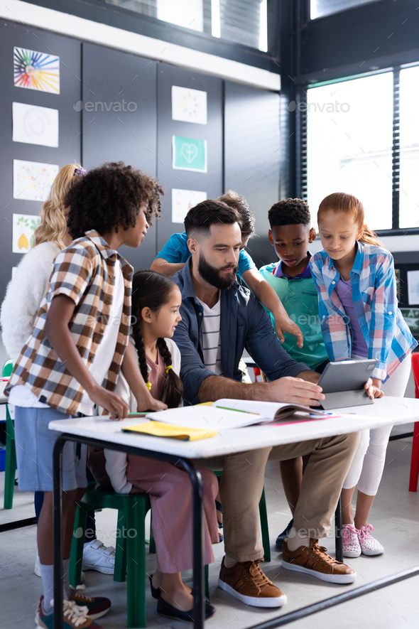 Vertical of diverse schoolchildren and male teacher using tablet ...