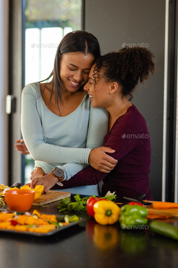 Happy Biracial Lesbian Couple Hugging And Chopping Vegetables In