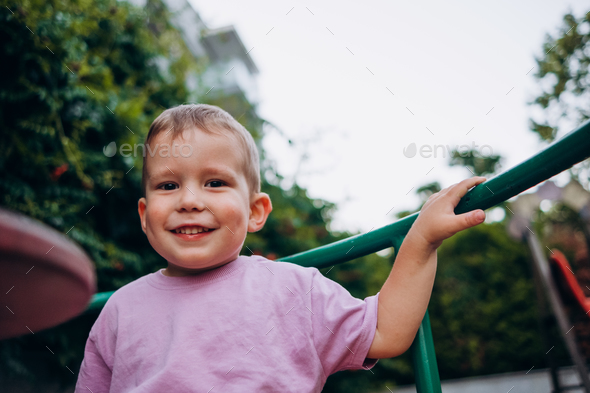 happy little boy spinning on a children's carousel in the playground ...