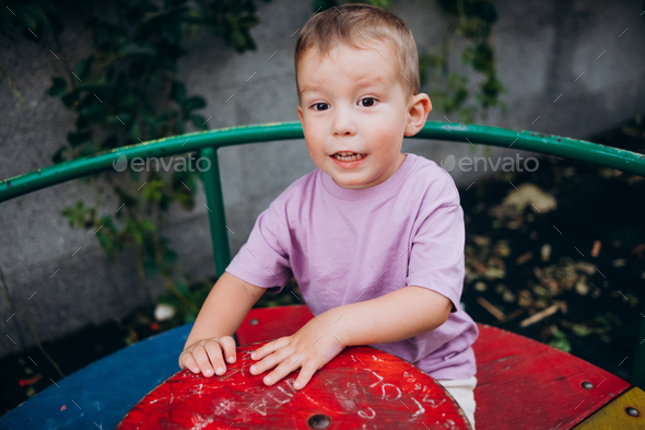 happy little boy spinning on a children's carousel in the playground ...