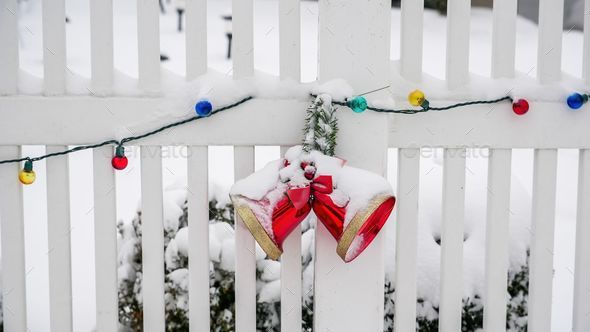 Red Christmas bells with lights on fence in winter Stock Photo by wirestock