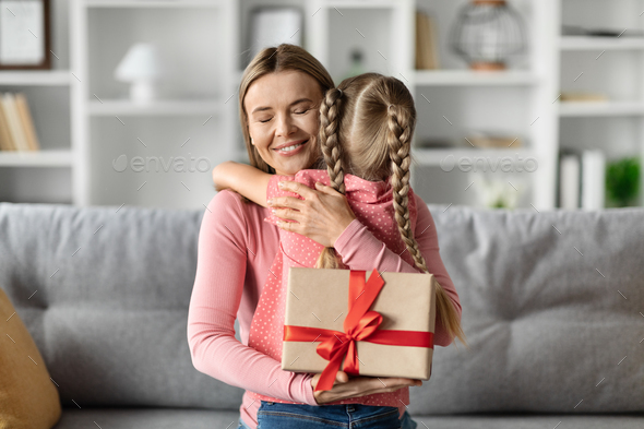 Cheerful young mother with gift box hugging her luttle daughter at home Stock Photo by Prostock ...