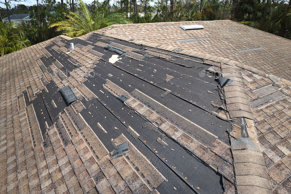 Wind damaged house roof with missing asphalt shingles after hurricane ...