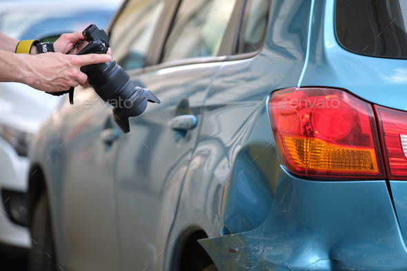 Insurance worker taking photo on camera of dented fender on street ...