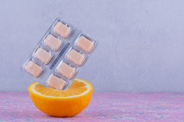 Half-sliced orange with a pack of chewing gum tablets on top on marble ...