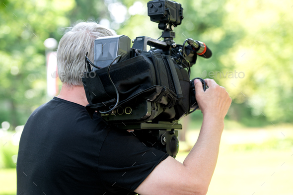 Side view of cameraman carrying camera on his shoulder Stock Photo by ...