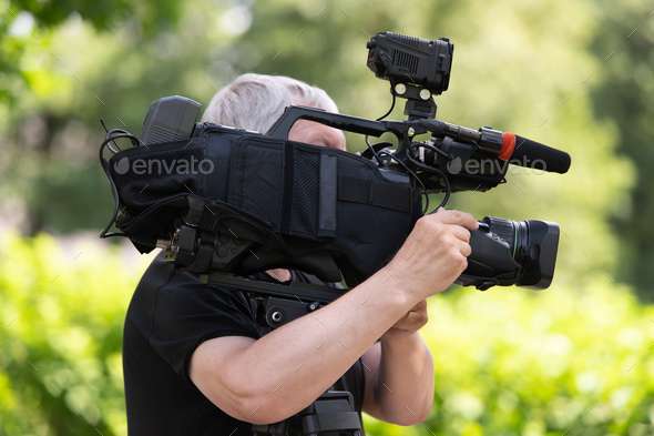 Side view of cameraman carrying camera on his shoulder Stock Photo by ...