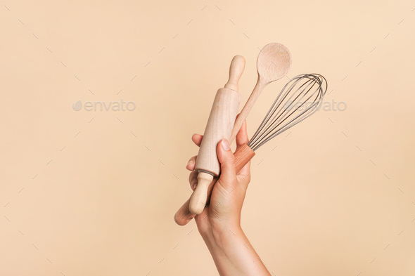 Female hand holding kitchen utensils for food and bakery on beige ...