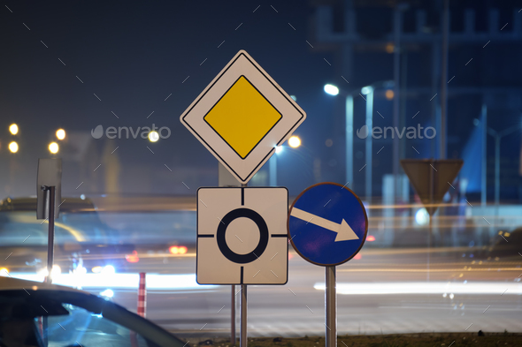 Roundabout road signs with blurred cars on city street traffic at night ...