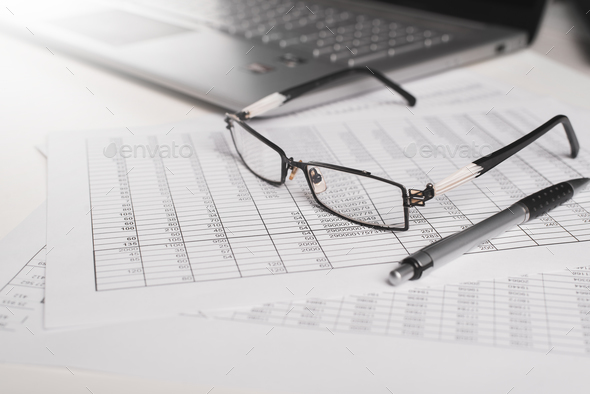 Invoices, accounting documents, pen, laptop and eyeglasses at the ...