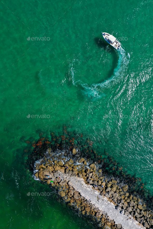 An aerial top view of a boat sailing in bright emerald green water ...