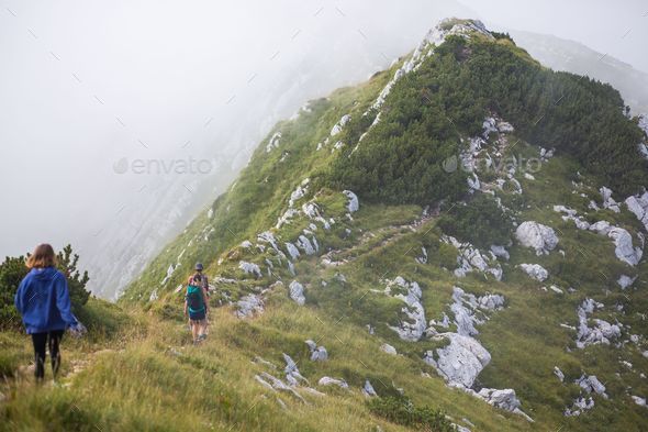People trekking up a steep incline towards a range of misty mountains ...