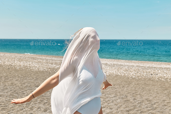 Pretty blond woman in swimsuit and white pareo enjoying sunny windy day ...