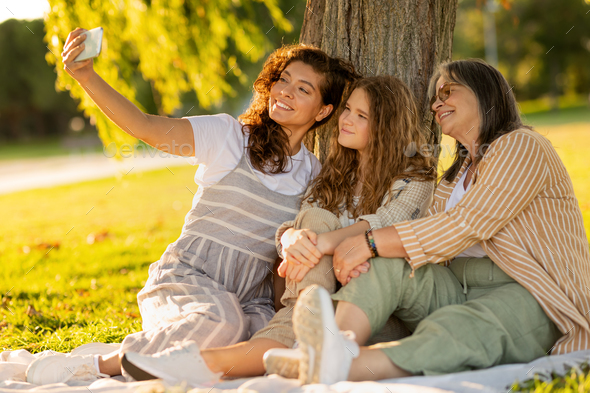 Cheerful caucasian multi-generation different women rest, enjoy picnic in park, take selfie on ...