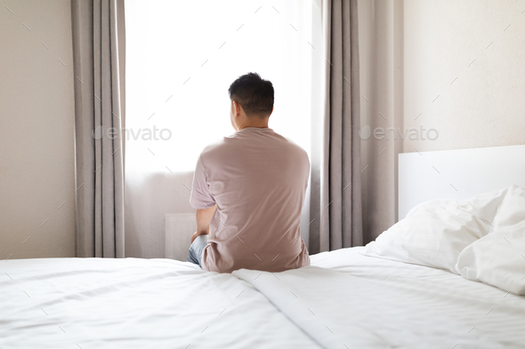 Back view of fully-rested man sitting on bed, enjoying morning Stock ...