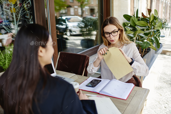 Excited young woman opening envelope while colleague watching Stock ...