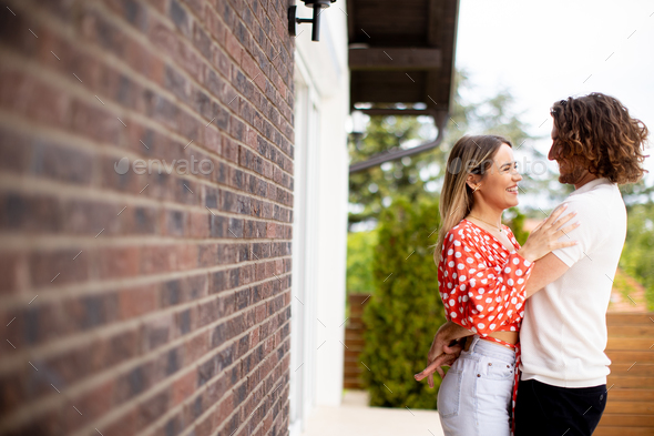 Smiling young couple in love standing in front of house brick wall ...
