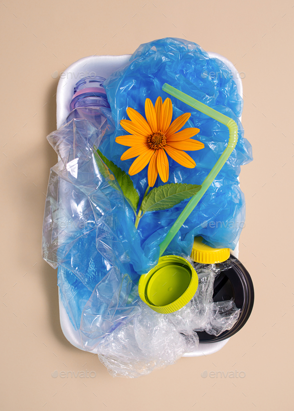 A flower in a plastic container with garbage on a beige background ...