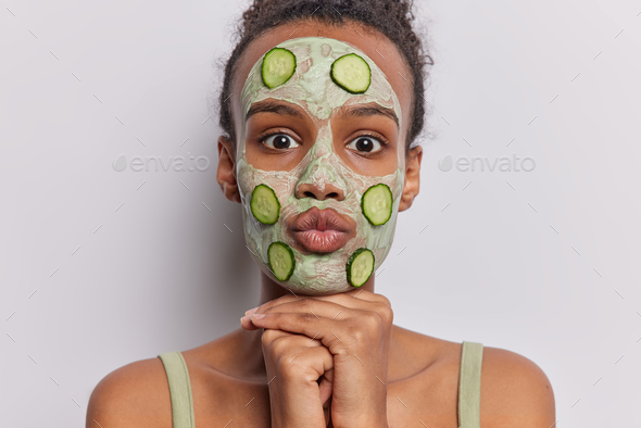 Photo Of Lovely Young Girl Keeps Hands Under Chin Lips Folded Applies Facial Clay Mask With