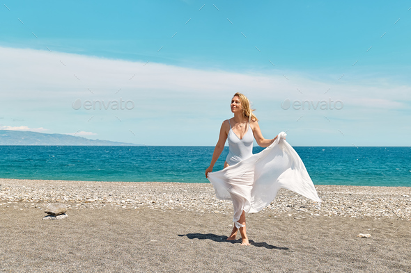 Pretty blond woman in swimsuit and white pareo enjoying sunny windy day ...