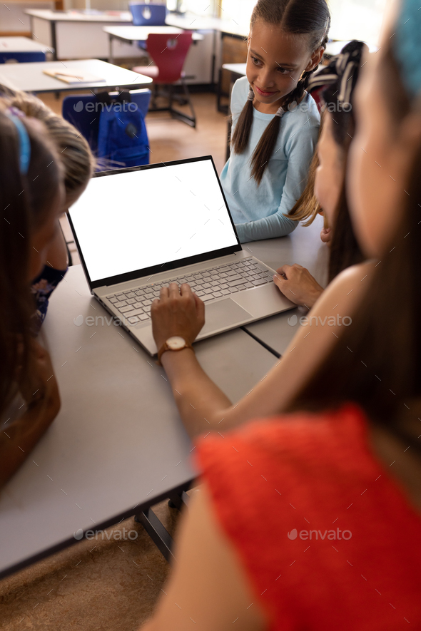 Diverse female teacher with laptop and elementary schoolgirls in class ...
