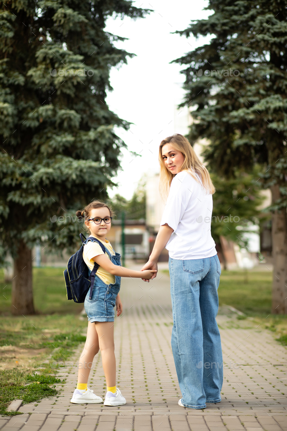 Mother and daughter pupil walking to school. Mom leads little school ...