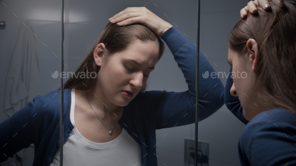 Upset and stressed woman standing at mirror in bathroom. Concept of ...