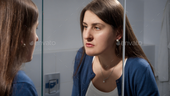 Upset frustrated woman feeling sad looking in her reflection in mirror ...