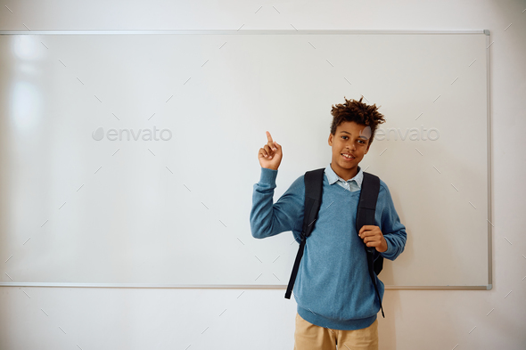 Happy black high school student pointing at whiteboard in the classroom ...