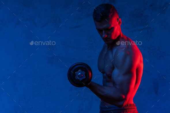 Muscular bodybuilder man exercising with a dumbbell in colorful neon ...