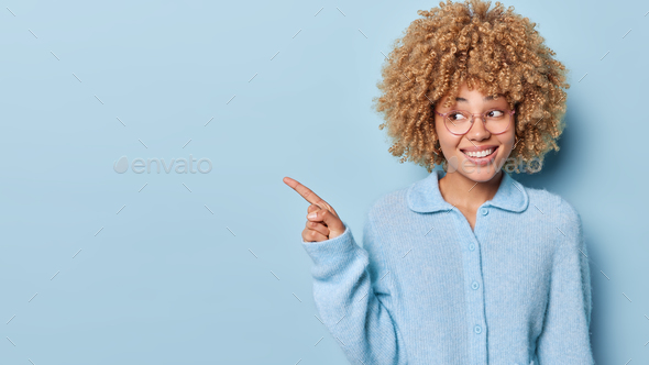 Horizontal shot of cheerful blonde curly young woman points index ...