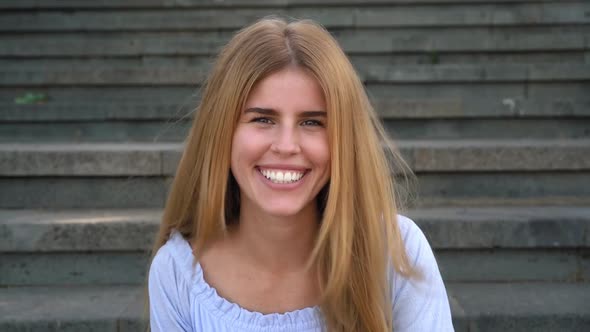 Happy young woman smiling into the camera while sitting on urban stairs ...