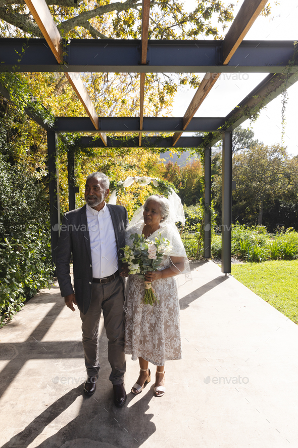 Happy senior biracial bride and groom holding hands at sunny outdoor ...