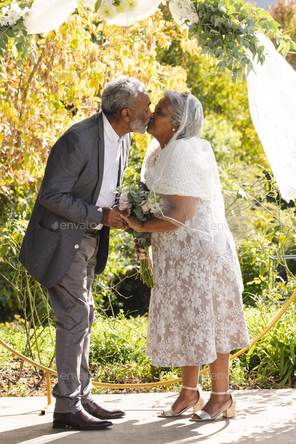 Happy senior biracial bride and groom kissing at wedding ceremony in ...