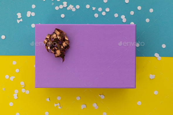 Purple gift box with ribbon and white confetti on yellow and blue ...