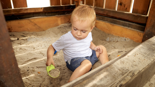 Cute little boy digging sand with toy shovel in sandbox at park. Kids ...