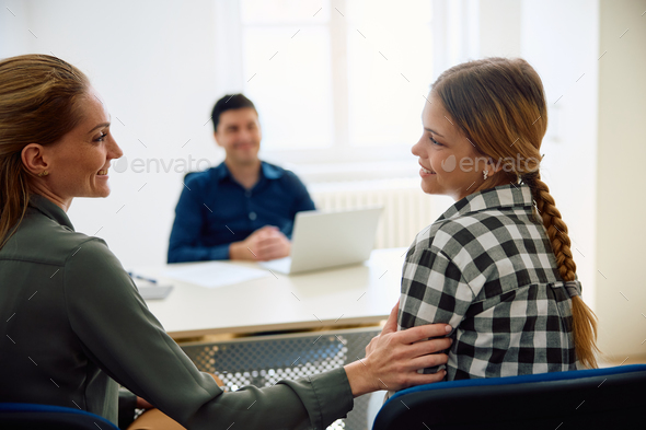 Happy teenage girl talking to her mother in the principal's office at ...