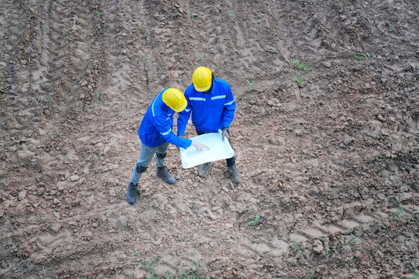 Top view two engineers discussing over blueprint on land at wind ...