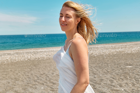 Pretty blond woman in swimsuit and white pareo enjoying sunny windy day ...