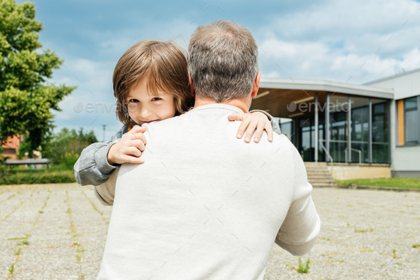 Satisfied son hugging his dad next to the school building after the end ...
