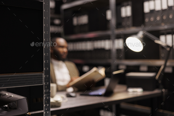 Detective working in dark room lit with desk lamp Stock Photo by DC_Studio