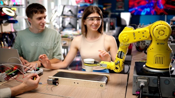 Three young happy engineers fixing an yellow robotic arm in the ...