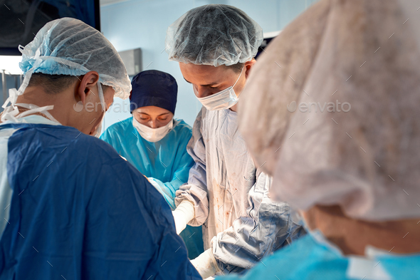 Portrait of surgeons leaned over patient during complex surgical ...