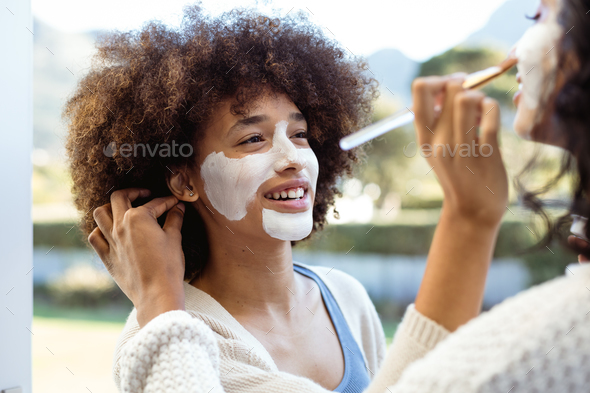 Smiling biracial female friends applying beauty cream on each others ...