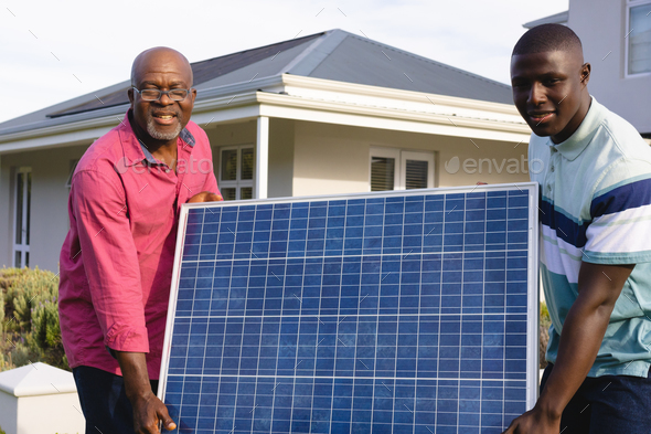 African american senior man with son carrying solar panel while ...