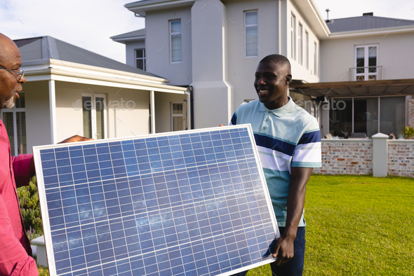 African american man with senior father carrying solar panel while ...