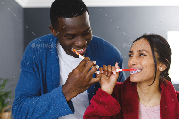 Happy diverse couple in brushing teeth in bathroom, looking at each ...